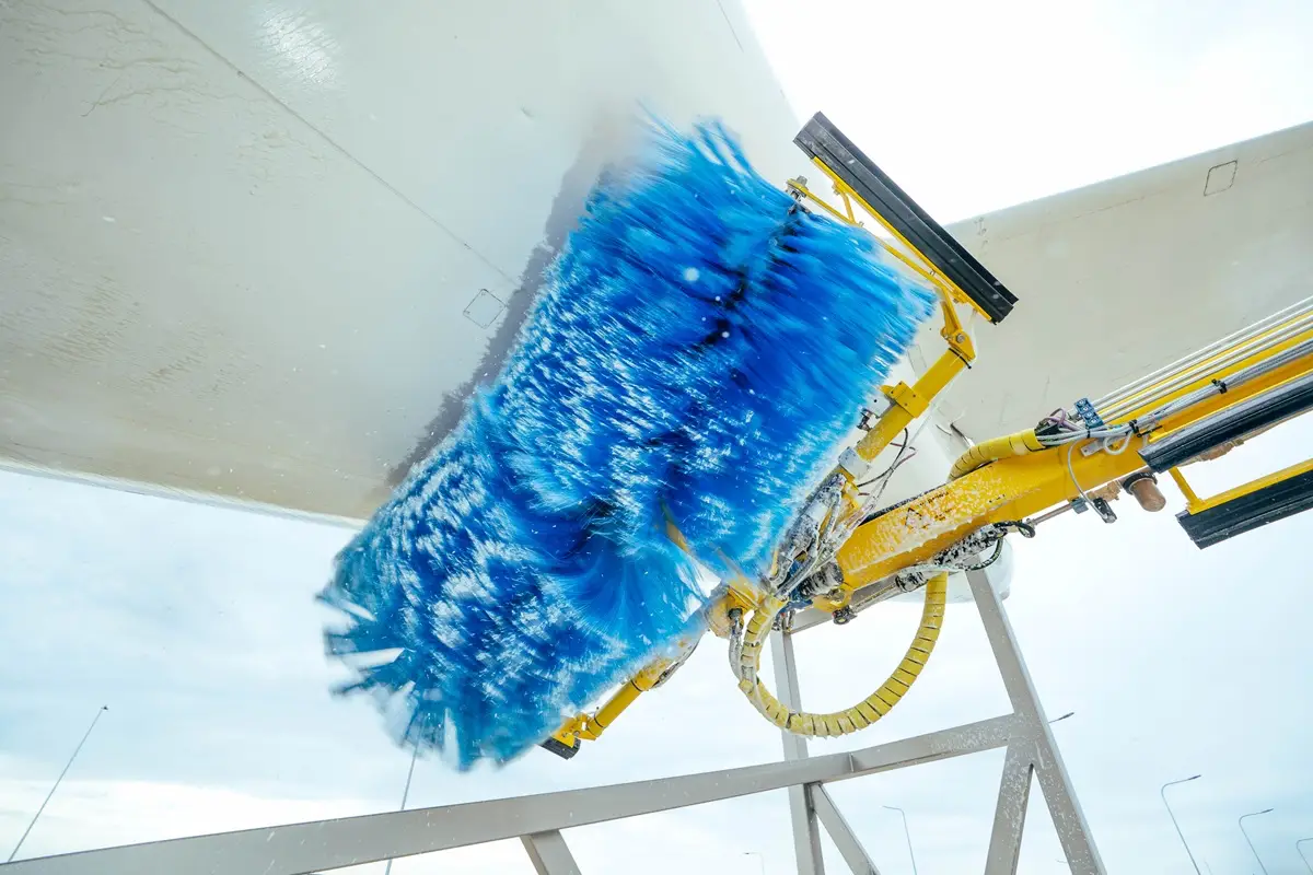 Robotic wet wash cleaning an aircraft wing with a blue rotating brush, showcasing modern automated aircraft maintenance.